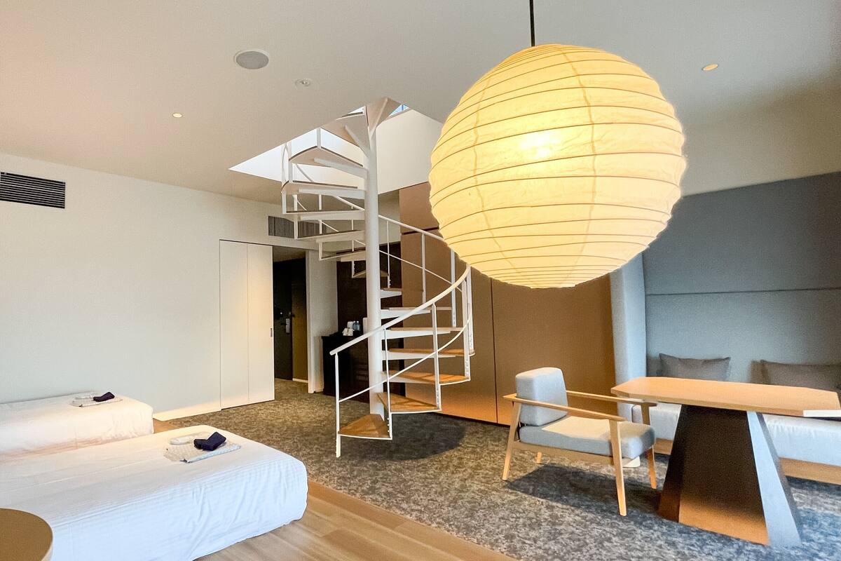 Quarto de hotel moderno com escadaria em espiral, área de jantar e um lustre grande.