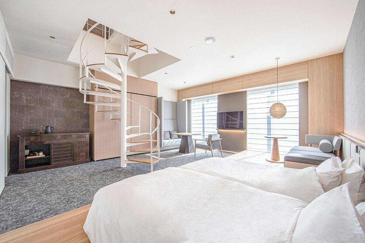 Quarto de hotel moderno com escada em espiral, uma cama grande, área de estar e vista para a cidade.
