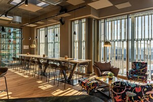 Um interior moderno com uma grande mesa de jantar, cadeiras e um sofá. Janelas amplas oferecem vista da cidade.