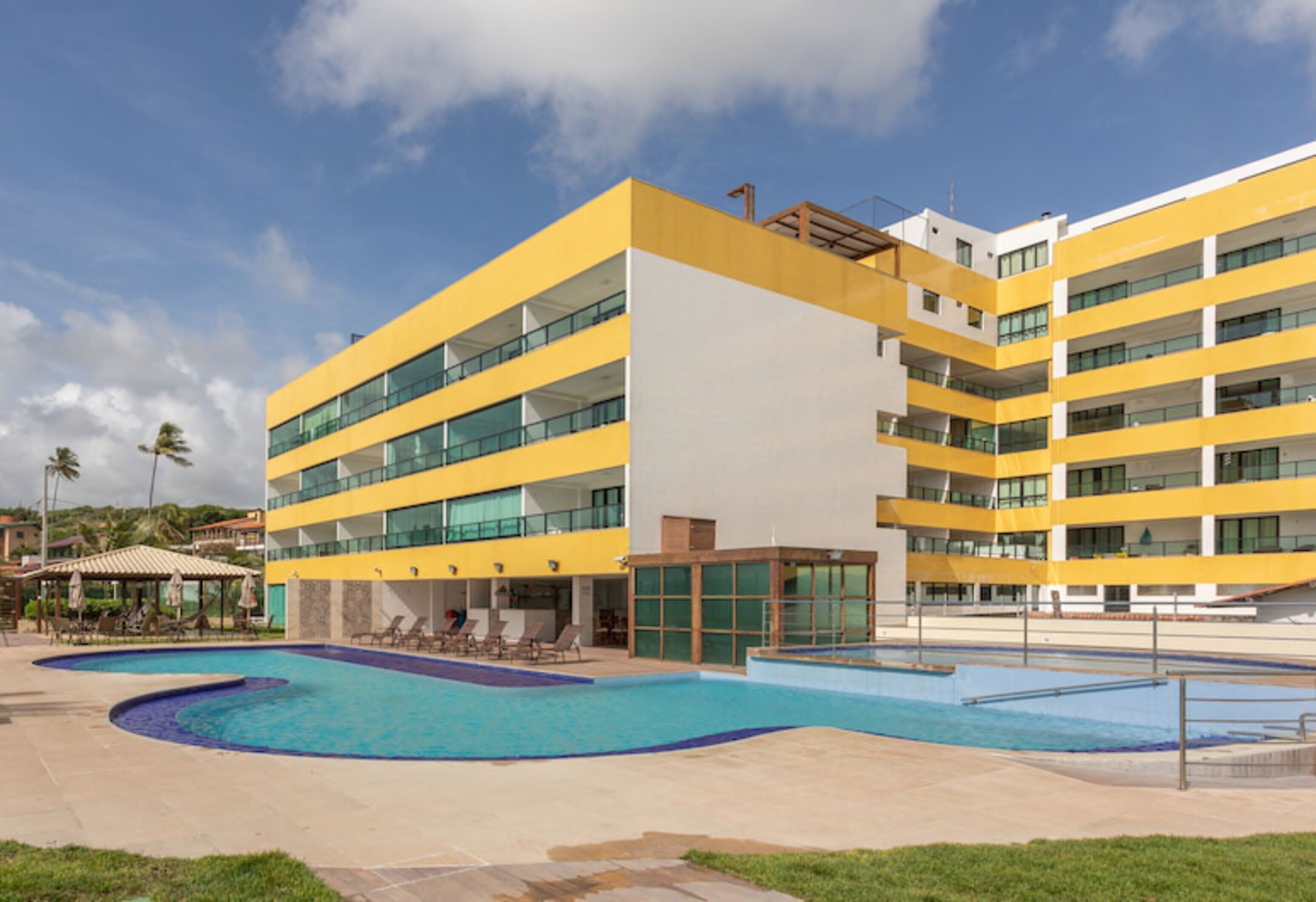 Um hotel moderno com piscina, várias varandas e um céu azul límpido.