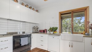 Uma cozinha moderna com armários brancos, forno embutido, lava-louças e uma janela com vista para árvores.