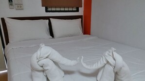 Cama bem arrumada com lençóis brancos e duas toalhas dispostas de forma decorativa.