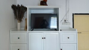 Uma unidade de entretenimento branca com uma TV de tela plana, uma estátua decorativa e um vaso com plantas secas.