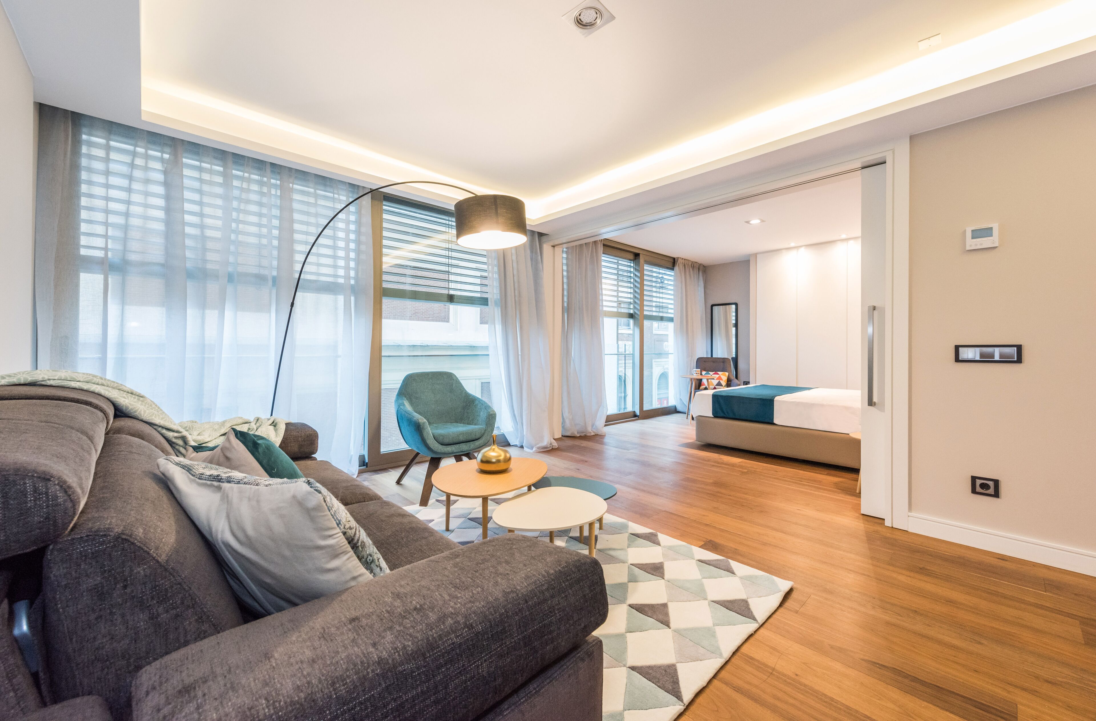 Quarto de hotel moderno com sofá, poltrona, mesa redonda pequena e uma cama.