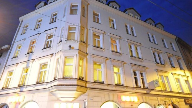 Um edifício de vários andares com estilo arquitetônico clássico, apresentando uma fachada simétrica e janelas e sacadas uniformemente distribuídas.