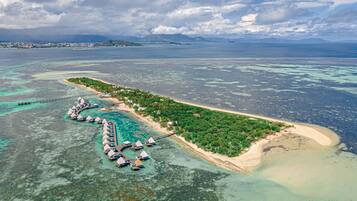 Vista aérea de uma ilha resort com bangalôs sobre a água, ligados por uma ponte.