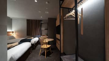 Quarto de hotel com duas camas, uma mesa pequena, uma cadeira, escrivaninha e um guarda-roupa.