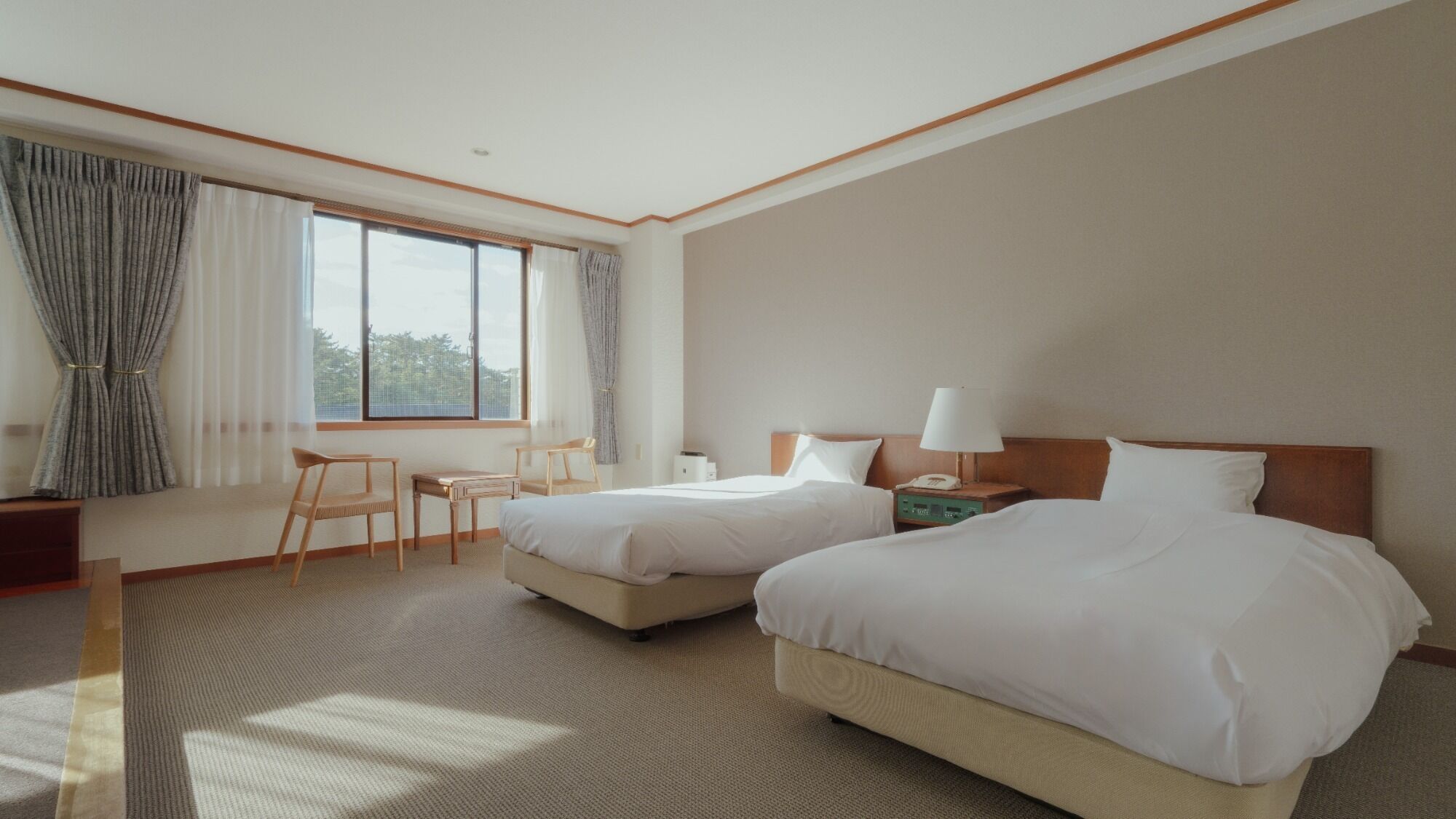Quarto de hotel com duas camas, uma escrivaninha, uma cadeira e uma janela com cortinas.