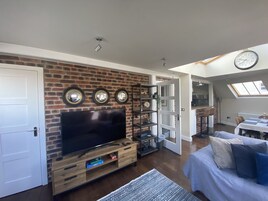 Uma sala de estar moderna com parede de tijolos, televisão de tela plana e área de jantar com teto alto e claraboia.
