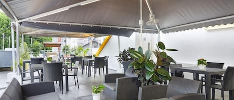 Área de varanda externa com móveis de vime, ventilador e plantas em vasos.