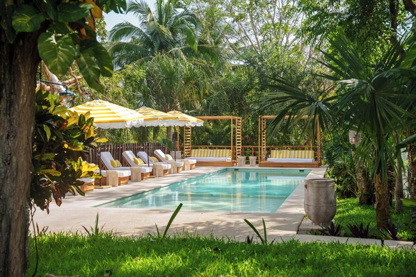 Área de piscina com espreguiçadeiras e guarda-sóis, rodeada por vegetação exuberante.