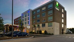Um edifício Holiday Inn Express com vários andares, um estacionamento com vários carros e um poste de luz.