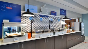 Disposição de buffet com estações de comida identificadas, um espaço para café e um dispensador de iogurte.