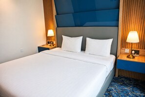 Quarto de hotel com uma cama grande, duas mesas de cabeceira com abajures e um tapete estampado.