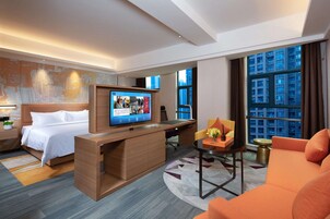 Quarto de hotel moderno com cama, escrivaninha, televisão e sofá.