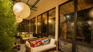 Uma área externa com assentos de vime, janelas amplas e luminárias esféricas penduradas.