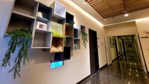 Um corredor moderno com estantes embutidas, algumas com plantas, e um sinal digital indicando uma saída.