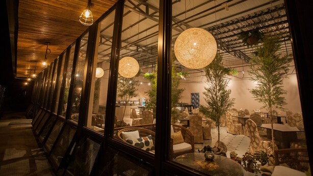 Interior moderno com grandes janelas, móveis de vime e luminárias esféricas pendentes.