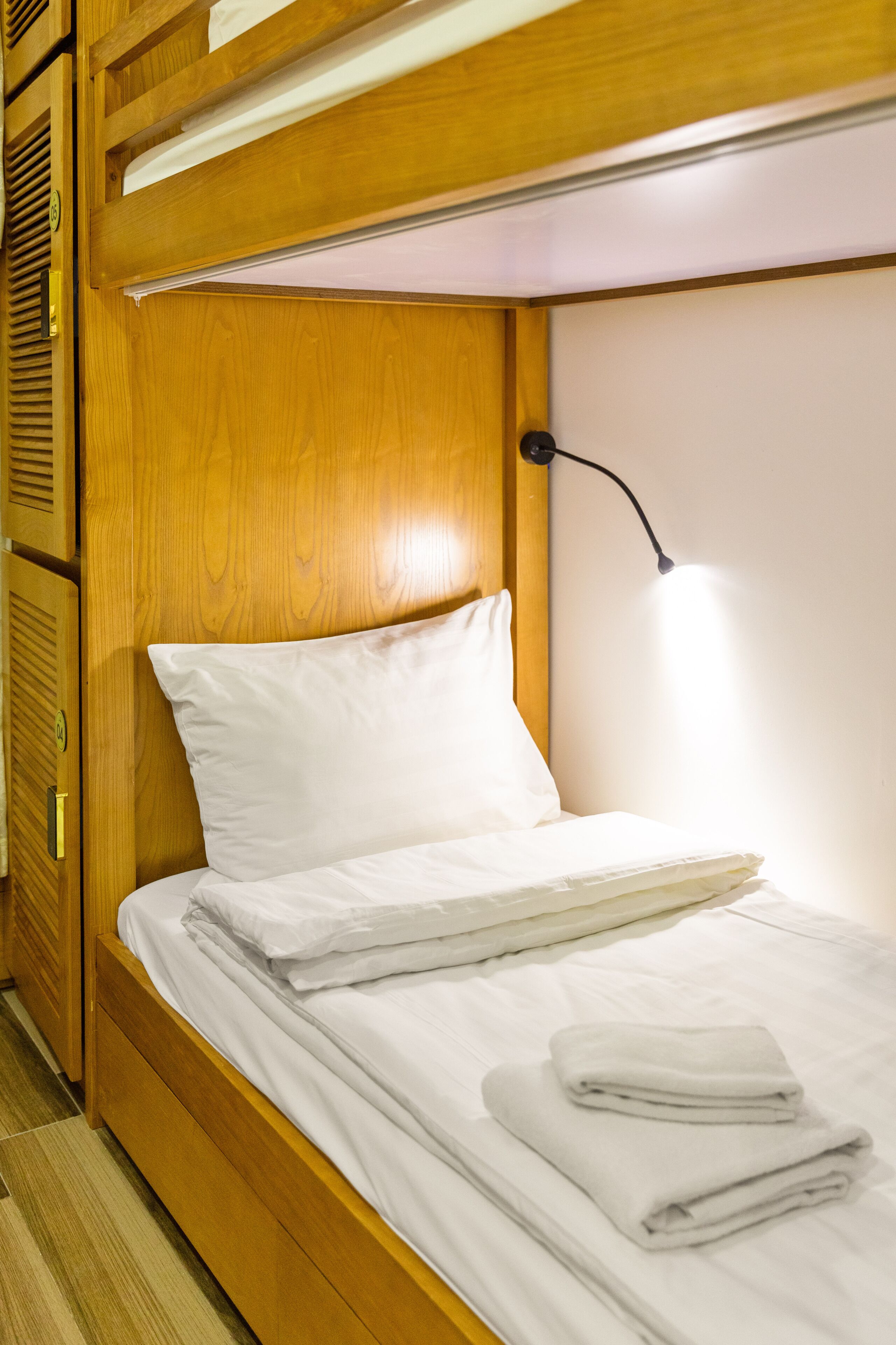 Uma cama de solteiro com roupa de cama branca e uma toalha dobrada na cama de baixo.