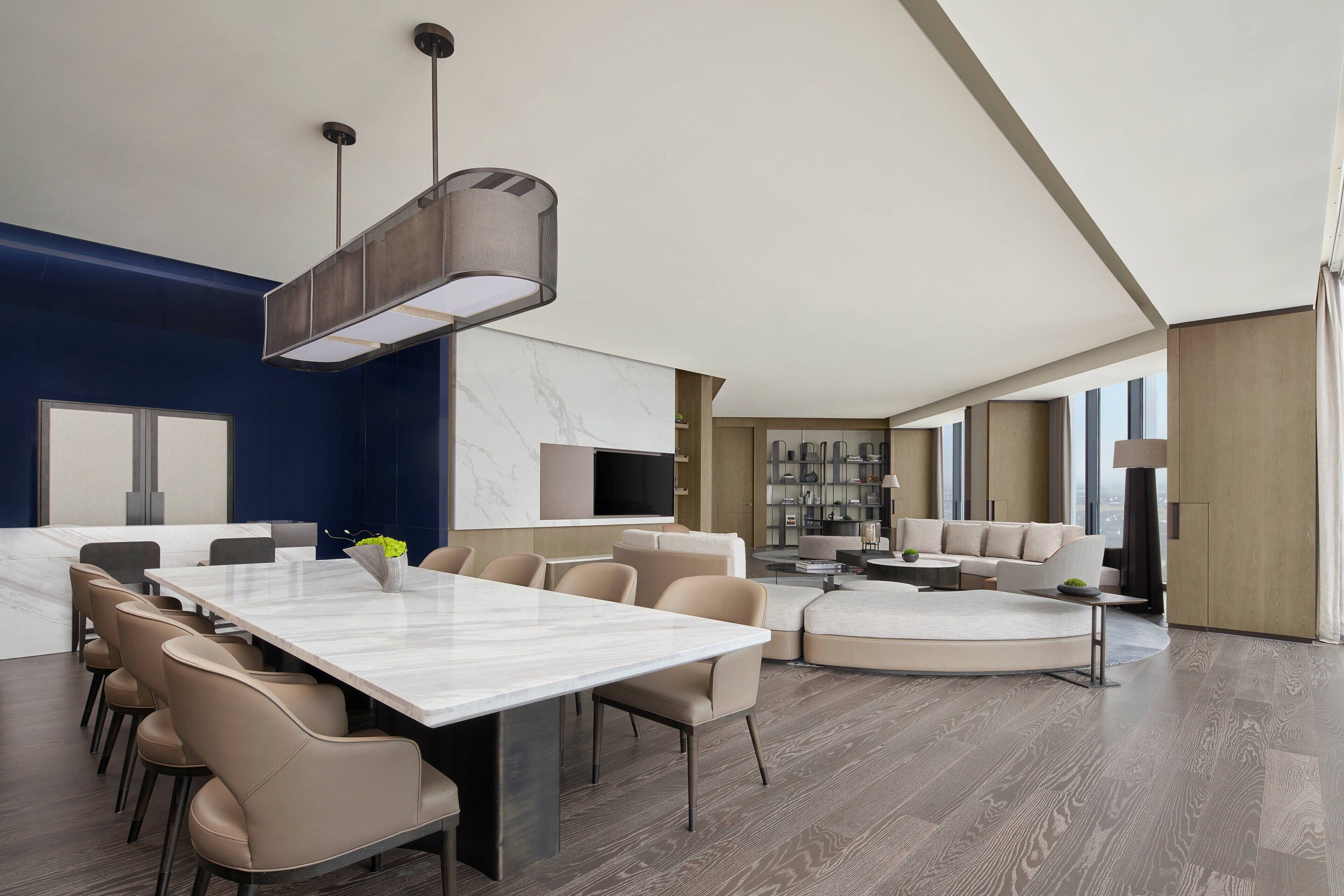Uma sala de estar moderna com um amplo sofá em formato de L, uma área de jantar com mesa de mármore e cadeiras, e uma janela grande que proporciona luz natural.