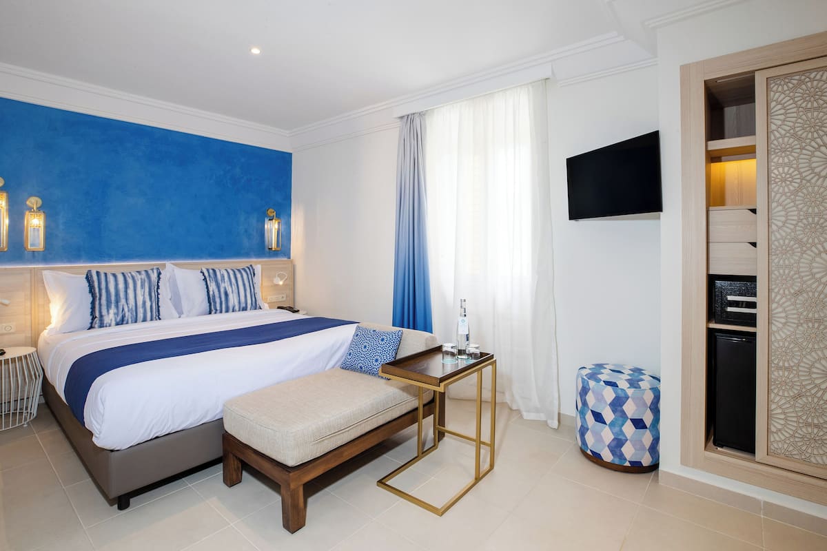 Quarto de hotel moderno com uma cama grande, mesas de cabeceira, televisão e um painel decorativo na parede.