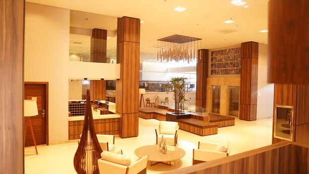 Um hall de hotel moderno, com detalhes em madeira, áreas de estar e uma planta central.