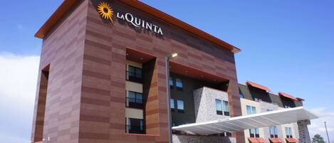 Um hotel La Quinta com design moderno, apresentando um sol proeminente no logotipo, uma entrada coberta e uma estrutura de vários andares com janelas e sacadas visíveis.