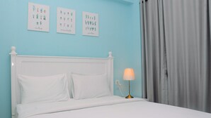 Cama bem arrumada com roupa branca, cabeceira branca e abajur.