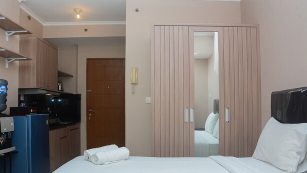 Quarto de hotel com cama, guarda-roupa, secretária com máquina de café e televisão.