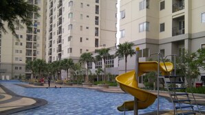 Piscina com escorregador amarelo e escada de metal, rodeada por palmeiras e edifícios residenciais.