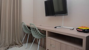 Quarto com escrivaninha, duas cadeiras, televisão e cortina.