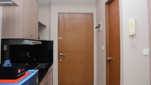 Uma cozinha compacta com fogão, pia e armários. Há uma porta de madeira e um telefone na parede.