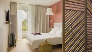 Quarto de hotel com cama, mala, sacola, televisão e janela com cortinas.
