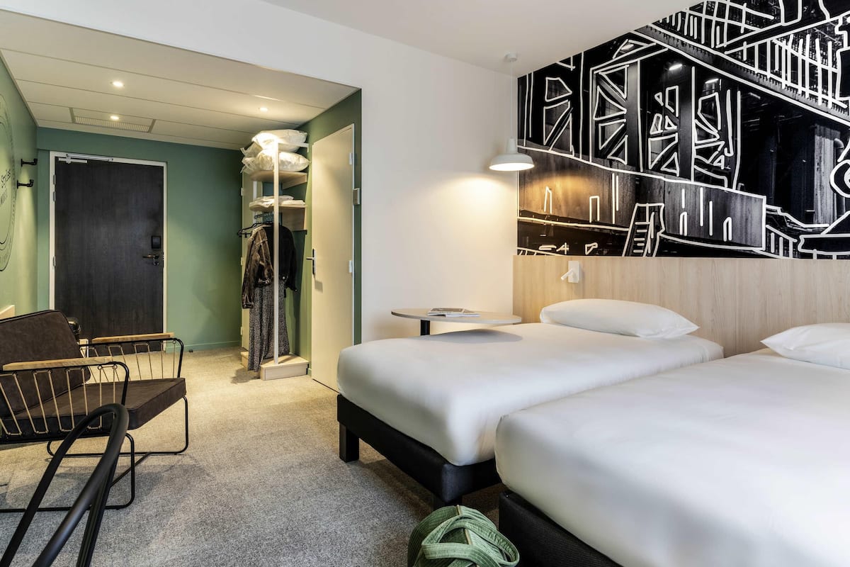 Quarto de hotel com cama, poltrona, escrivaninha e guarda-roupa.