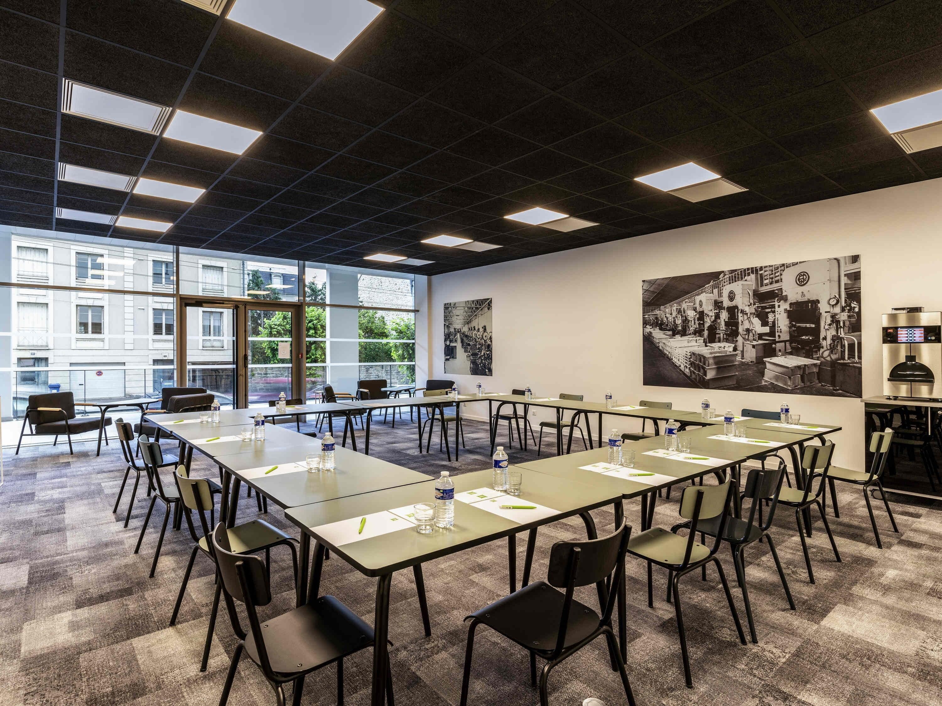 Sala de conferência com mesas de vidro, cadeiras e grandes janelas.