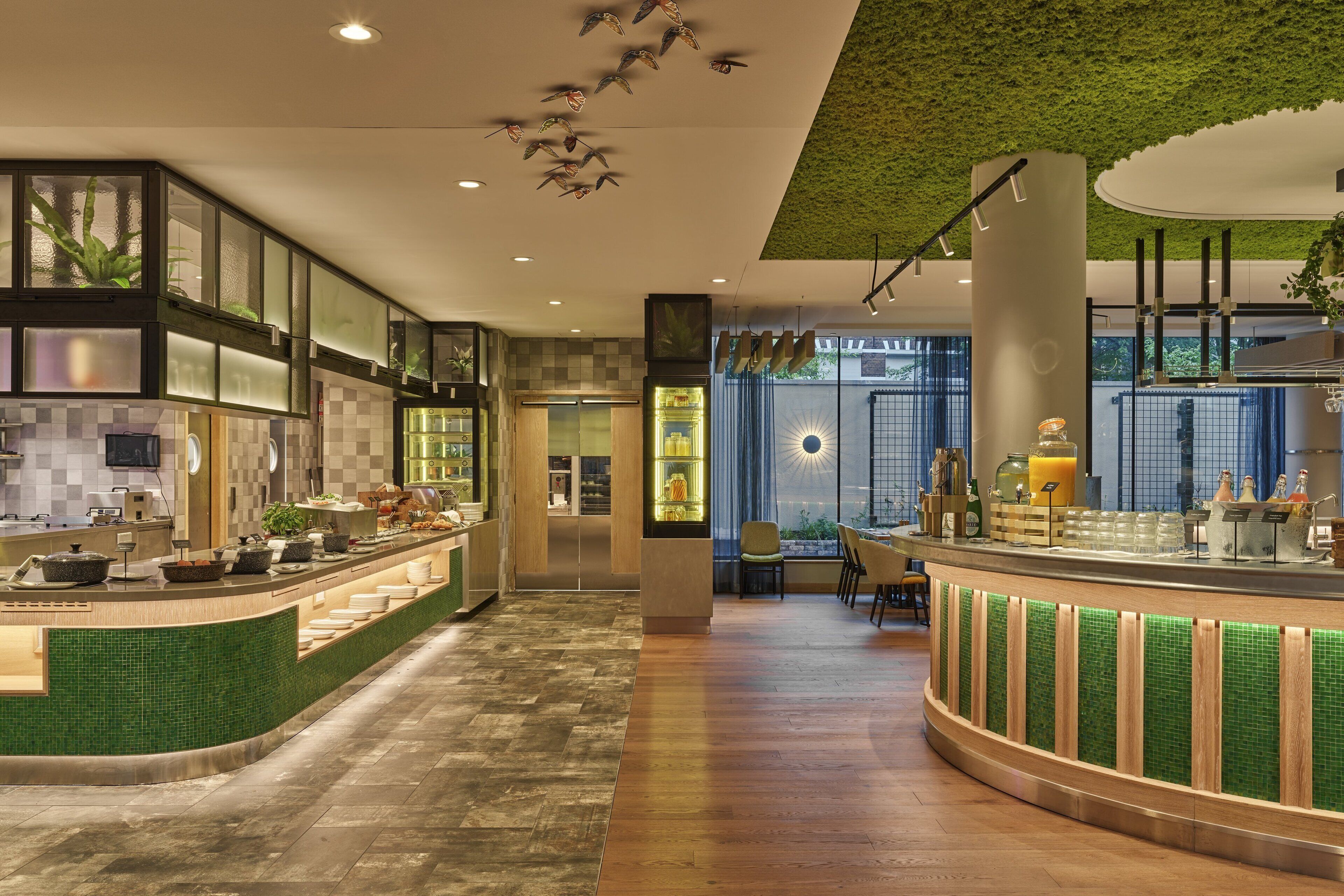 Um restaurante moderno com balcão curvo, área de bar com azulejos verdes e teto com luminárias pendentes.