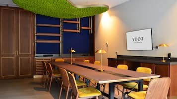 Uma sala de conferências com uma mesa comprida, cadeiras amarelas, um armário de madeira e uma parede azul.