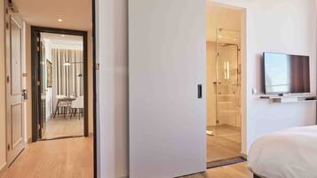 Quarto de hotel moderno com porta deslizante, TV fixada na parede e banheiro com box de vidro.