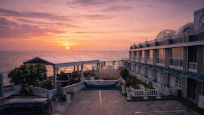 Um hotel à beira-mar com área de estar coberta ao ar livre, piscina e vista para o pôr do sol sobre o oceano.