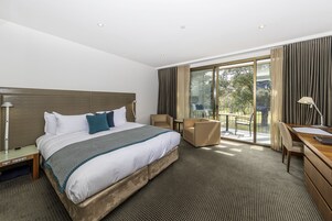 Quarto de hotel com uma cama grande, uma escrivaninha, uma cadeira e uma varanda com vista para o exterior.