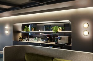 Uma área de bar moderna com design elegante, apresentando um balcão, garrafas de vinho, copos e uma máquina de café.
