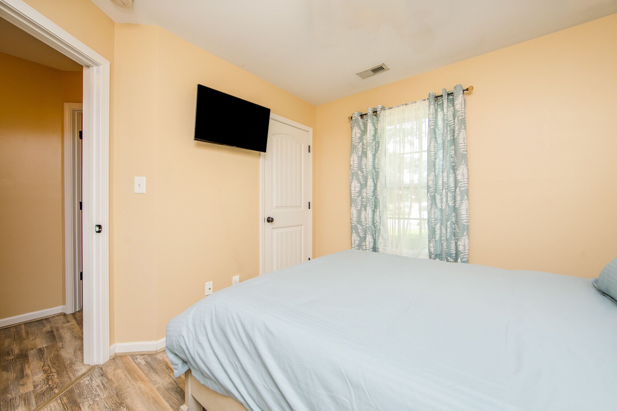 Quarto com uma cama, televisão na parede e janela com cortinas.