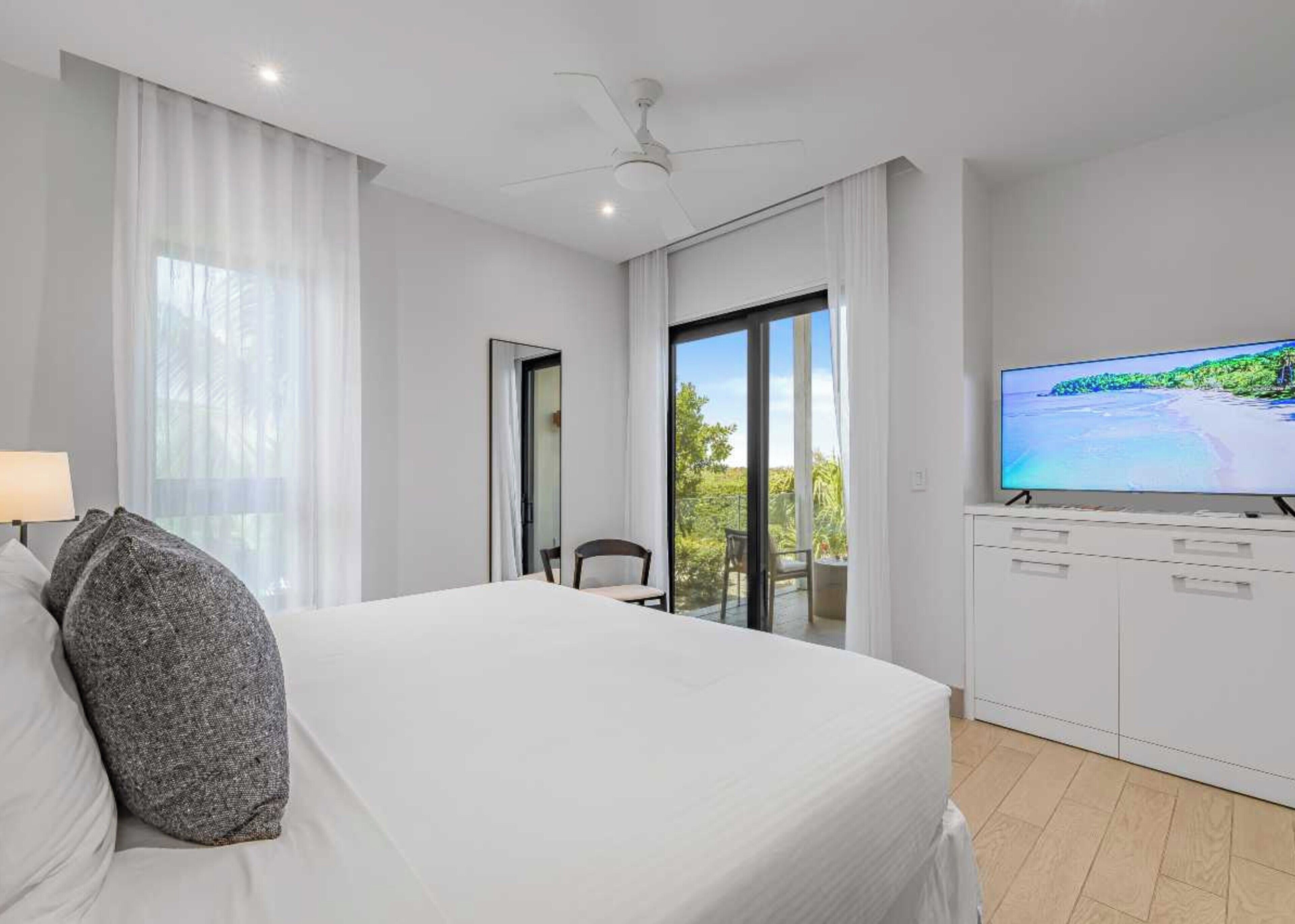 Quarto de hotel moderno com uma cama grande, televisão e varanda com vista para vegetação.