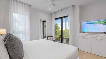 Quarto de hotel moderno com uma cama grande, televisão e varanda com vista para vegetação.