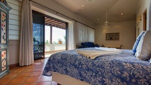 Quarto com uma cama grande, ventilador de teto e vista para o exterior por uma porta deslizante.