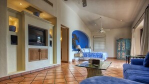 Uma sala de estar ampla com uma televisão grande, um ventilador de teto e um sofá azul.