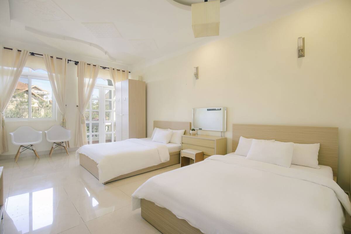 Quarto de hotel com duas camas, uma escrivaninha, uma cadeira, uma televisão e uma janela com cortinas.