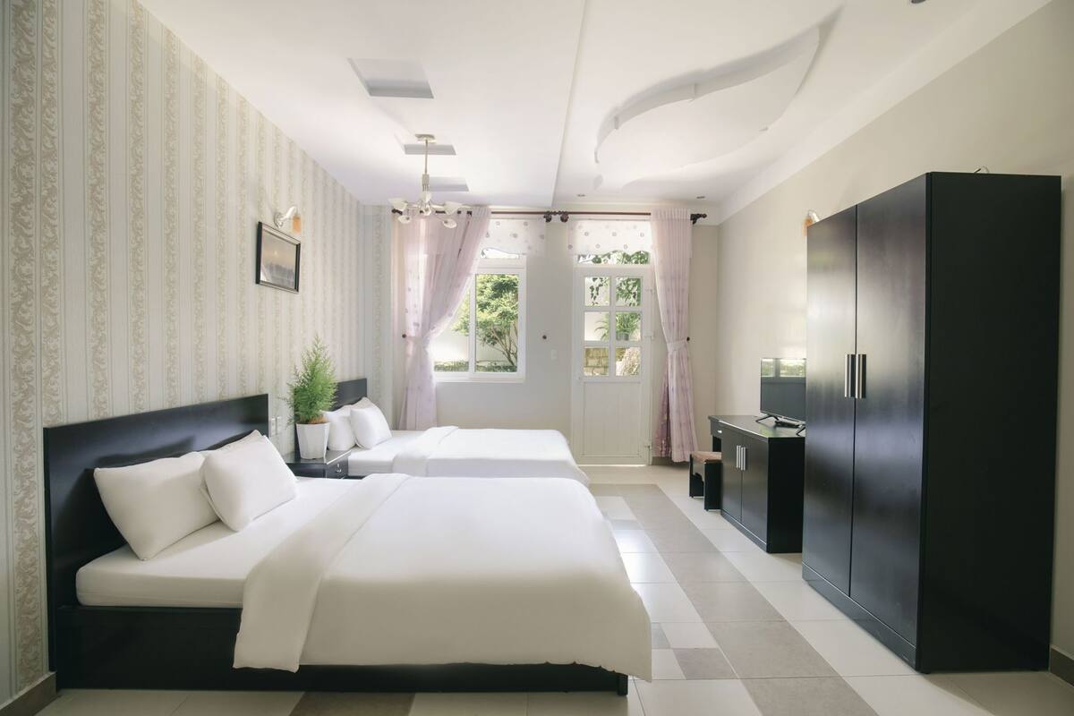 Quarto com duas camas, guarda-roupa, televisão e janela com cortinas.