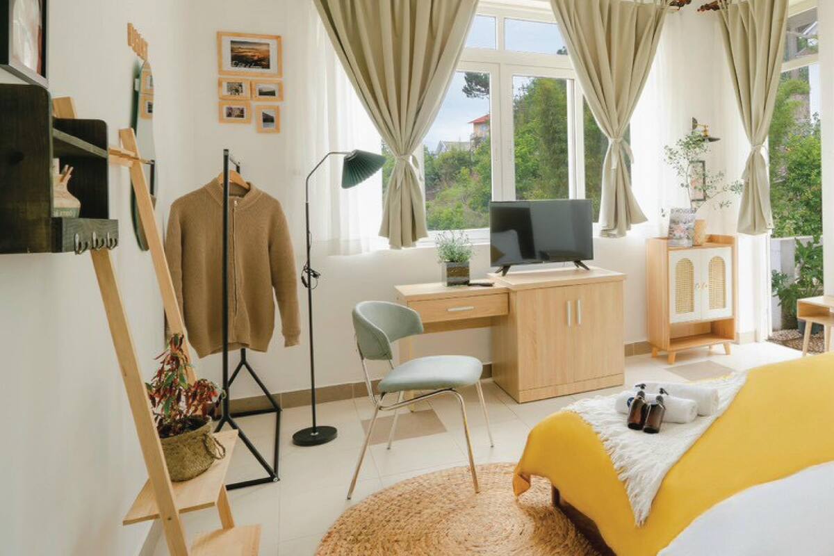 Quarto moderno com cama, escrivaninha e cadeira, janelas amplas com cortinas e vista para o verde lá fora.