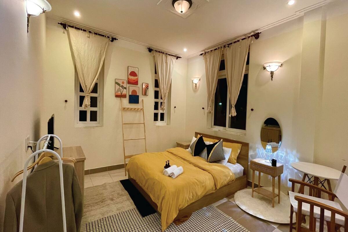 Quarto de hotel com cama, escrivaninha, cadeira, espelho e janela com cortinas.